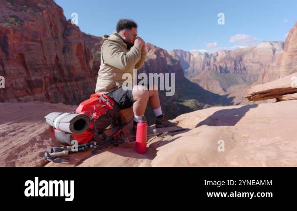 Hiker pauses for a refreshing drink while seated on a sturdy rock in ...