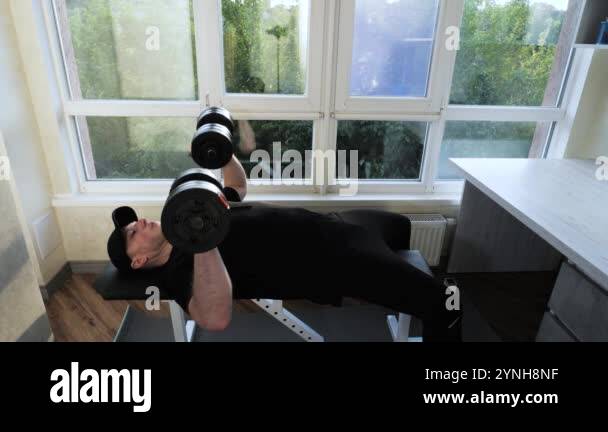 Dumbbell bench press in the home gym. Young man pumping chest muscles ...
