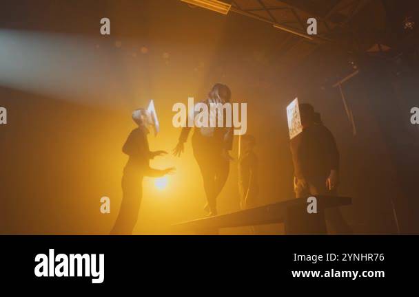 Three performers on a balance beam in a dramatic stage setting ...