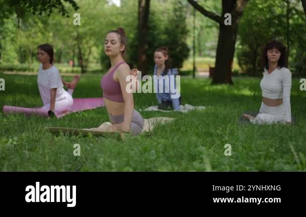 A group of women performing the Seated Spinal Twist pose during an outdoor yoga session in a ...