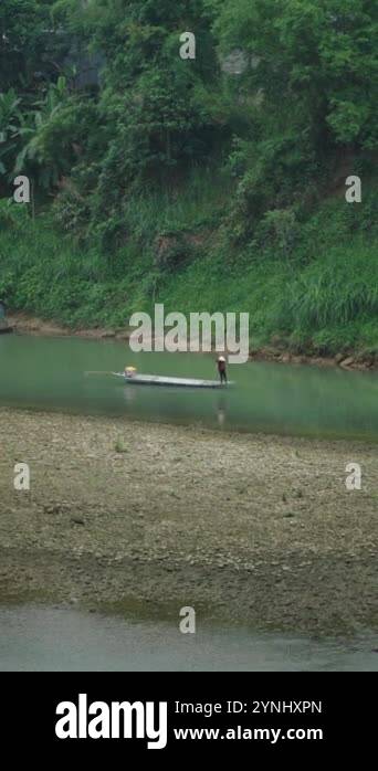 Fisherman standing on a small boat rowing with a big paddle on a river ...