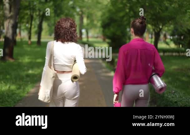 Back view of two women walking along a shaded park path, showcasing ...