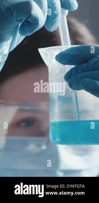 A researcher in PPE examines a test tube with vibrant blue liquid ...