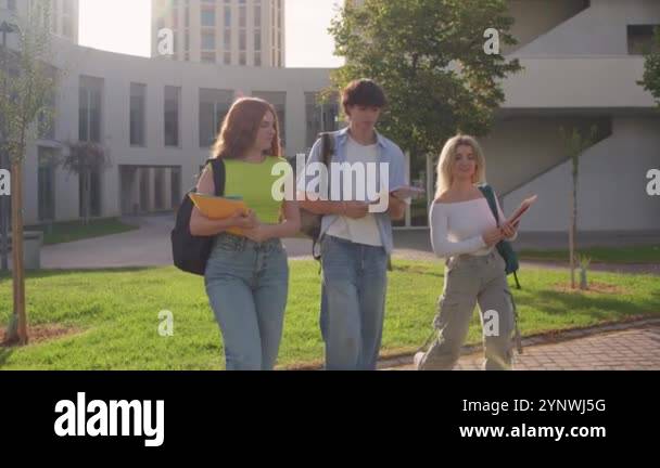 Three students are walking together on their university campus, engaged ...