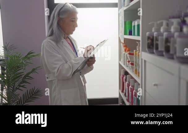 Woman taking notes on a clipboard in a pharmacy, surrounded by shelves ...