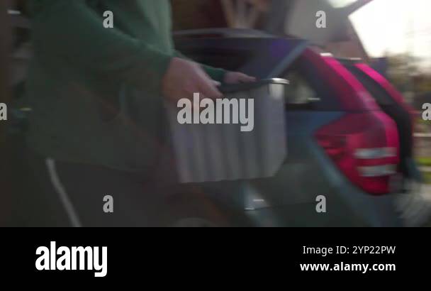 Man carrying a plastic storage box and placing it into car trunk ...