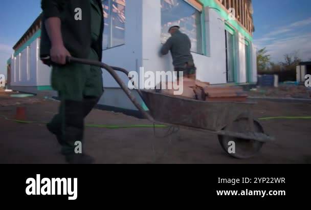 Man pushing a wheelbarrow loaded with wooden materials on a ...