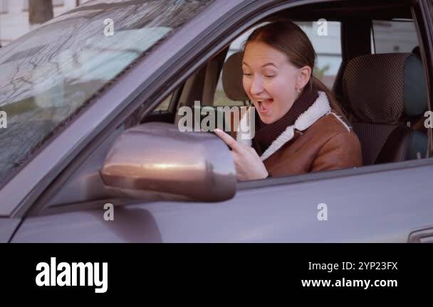Young woman driving car glances at her smartphone, expressing surprise ...