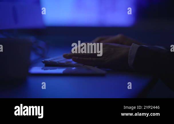 A closeup view of hands intently typing on a keyboard inside a dimlylit ...