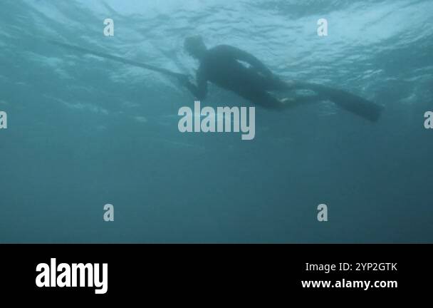 A low angle shot captures a man swimming underwater while gripping a ...