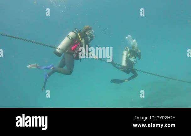 Two scuba divers pulling themselves along a chain underwater ...