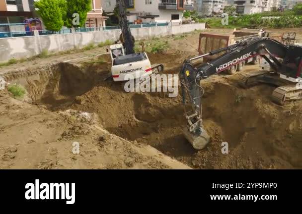 Fly over a dynamic construction site with an excavator and trucks ...
