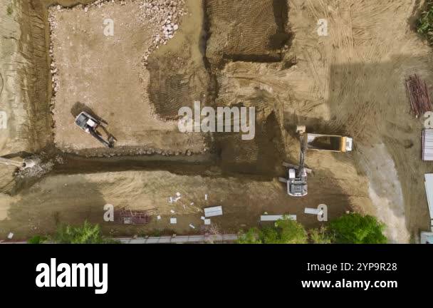 Fly over a construction site where an excavator loads soil into a truck ...
