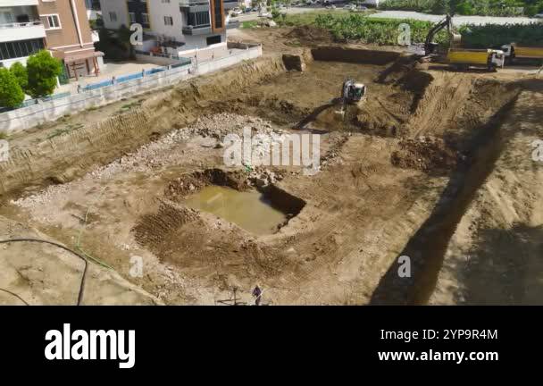Watch an excavator load soil into trucks at a busy construction site ...
