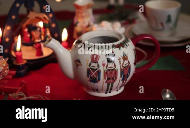 Hand put red cap atop Christmas teapot with nutcrackers pattern closeup ...