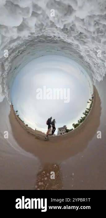 Vertical video. Two people stroll by the edge of the water, captured ...
