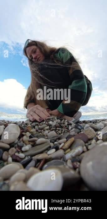 Vertical video. Low-angle close-up of a woman crouching on a pebble ...