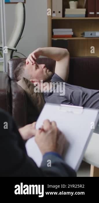 Vertical shot of man lying on couch, while rubbing his forehead and ...
