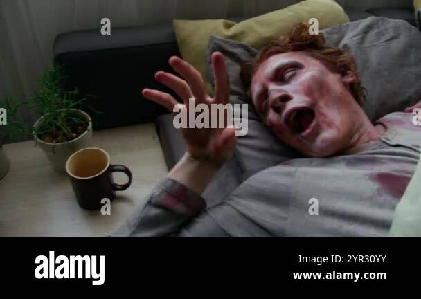 Medium tracking shot of young bloodied male zombie with white eyes ...