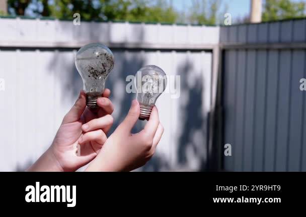 Two dirty incandescent light bulbs held up against a blurred fence and ...