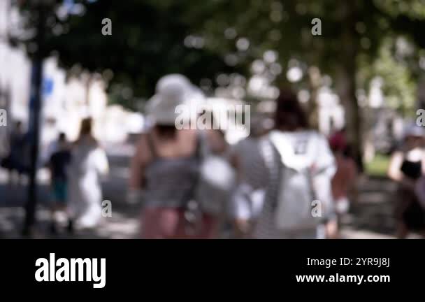 Blurred view of a summer city street with pedestrians and trees. Two ...