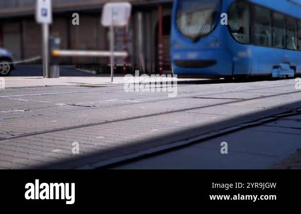 A low-angle view of a blue tram passing by, showcasing its wheels and ...