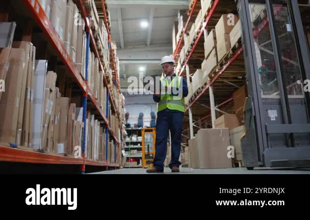 Logistics employee in a safety vest and helmet uses a laptop to verify ...