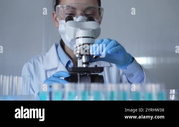 Scientist woman, wearing a lab coat, mask, blue gloves and safety glasses, is adjusting a ...