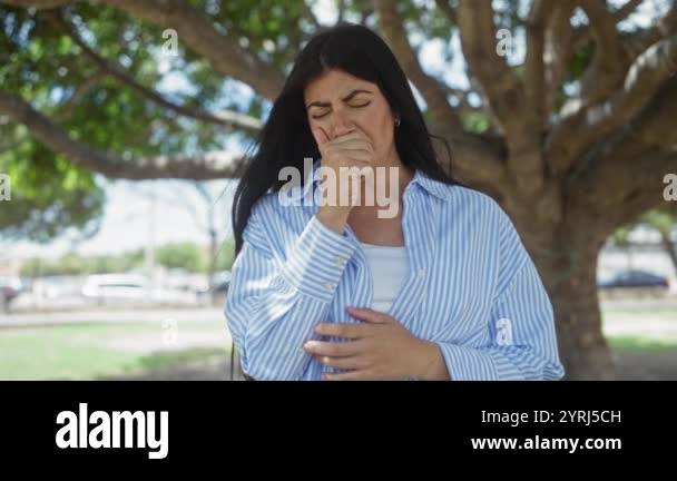 A young brunette hispanic woman feeling unwell in a park, holding her ...
