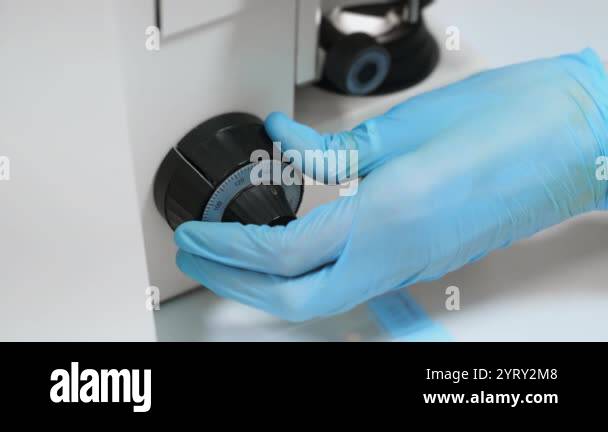 A medical laboratory worker wearing gloves turns the microscope ...