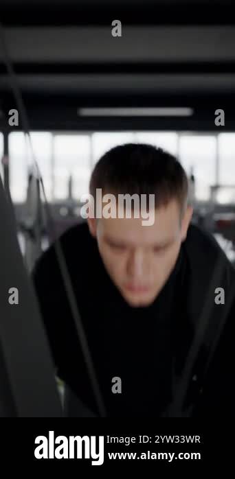 Focused young man engaged in strength training with a cable machine at a well-equipped indoor ...