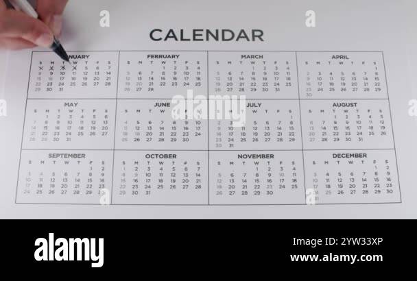 A person marks days on a yearly calendar with a pen, indicating ...