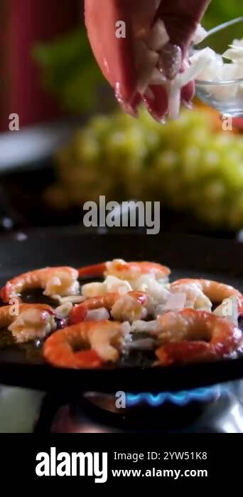 Professional chef roasts and tosses prawns in black frying pan with ...