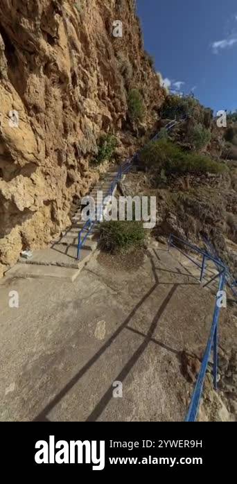 Vertical video. A woman descends the stone steps toward the edge of a ...