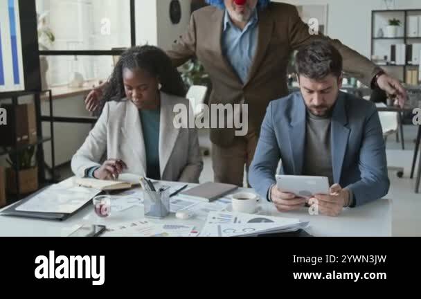 Group portrait of clown boss wearing blue wig and red nose embracing ...