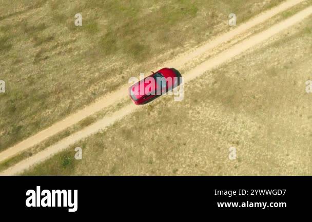 A red car drives through the ruts of a dusty dirt road across wild ...