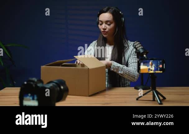 A fashion blogger opens a package during a live stream, revealing trendy clothes like sweater ...