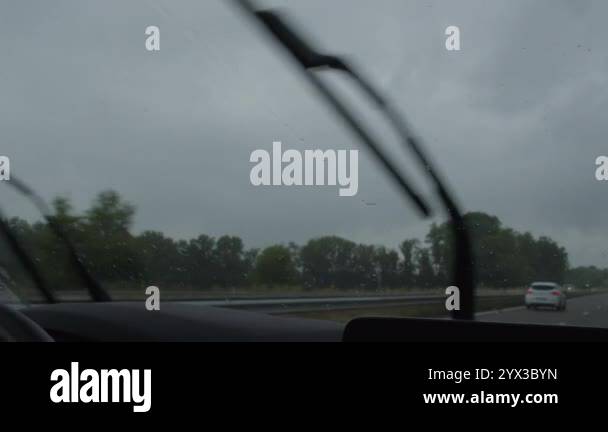 Windshield wipers working during a drive on a rain-soaked highway, with ...