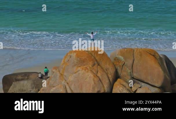 Young guy standing on huge stones on the shore of the Atlantic Ocean on ...