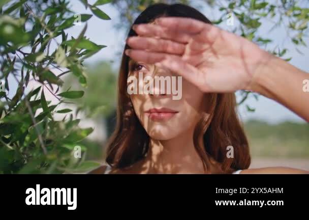 Closeup girl looking sunshine covering with hand in garden. Portrait of brunette enjoy fresh ...