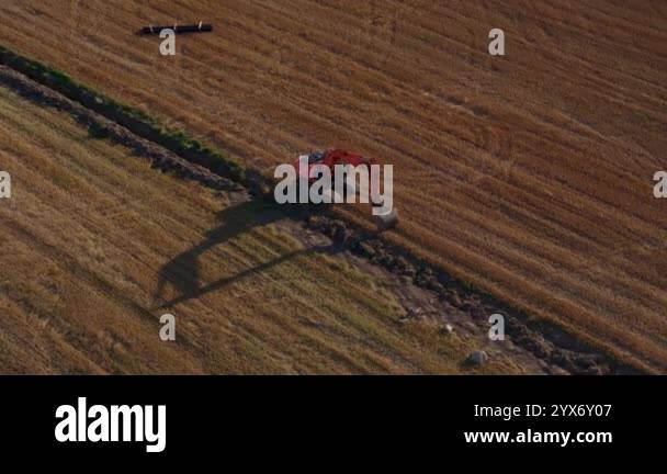 A large red excavator is actively digging a deep trench in an open ...