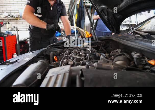 Young repairman working under hood of vehicle at service. Professional ...