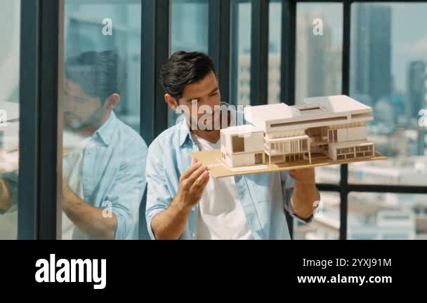 Skilled smiling caucasian engineer turns house model left and right to check mistake point ...