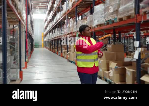 Warehouse worker scanning packages on shelves in a large facility ...