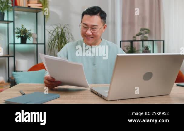 Happy Asian man freelancer work with documents at home analyzing ...