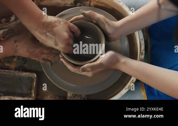 Cropped arms of two people working on modelling shape of raw clay ...