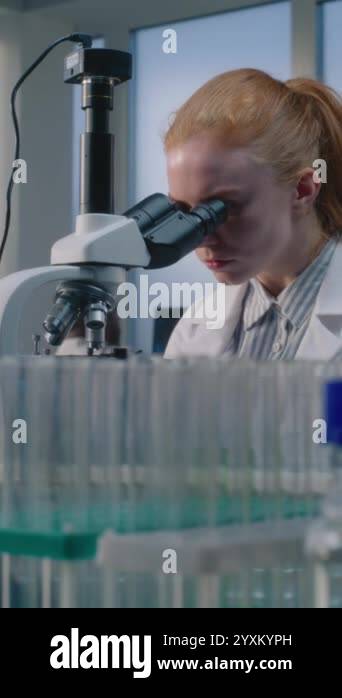 Vertical shot Professional microbiologist uses laptop, looks under ...