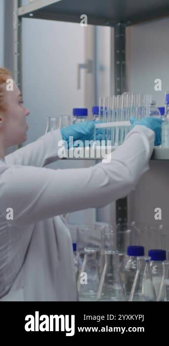 Vertical shot Female chemist in white coat takes test tubes for ...