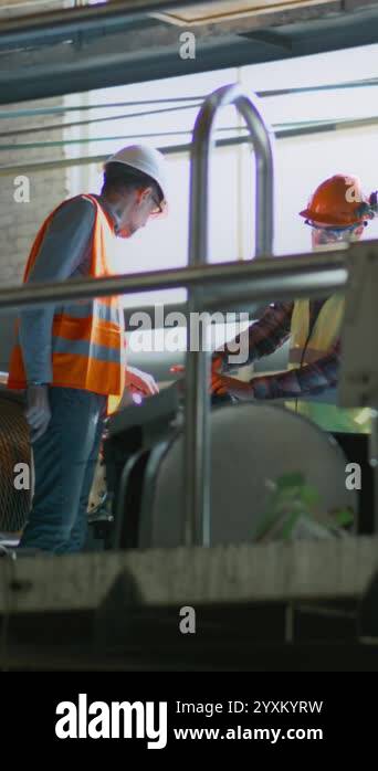 Two professional heavy industry engineers in protective uniforms and helmets at manufacturing ...