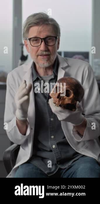 Mature lab worker or scientist speaks to camera, shows fossil skull of ...